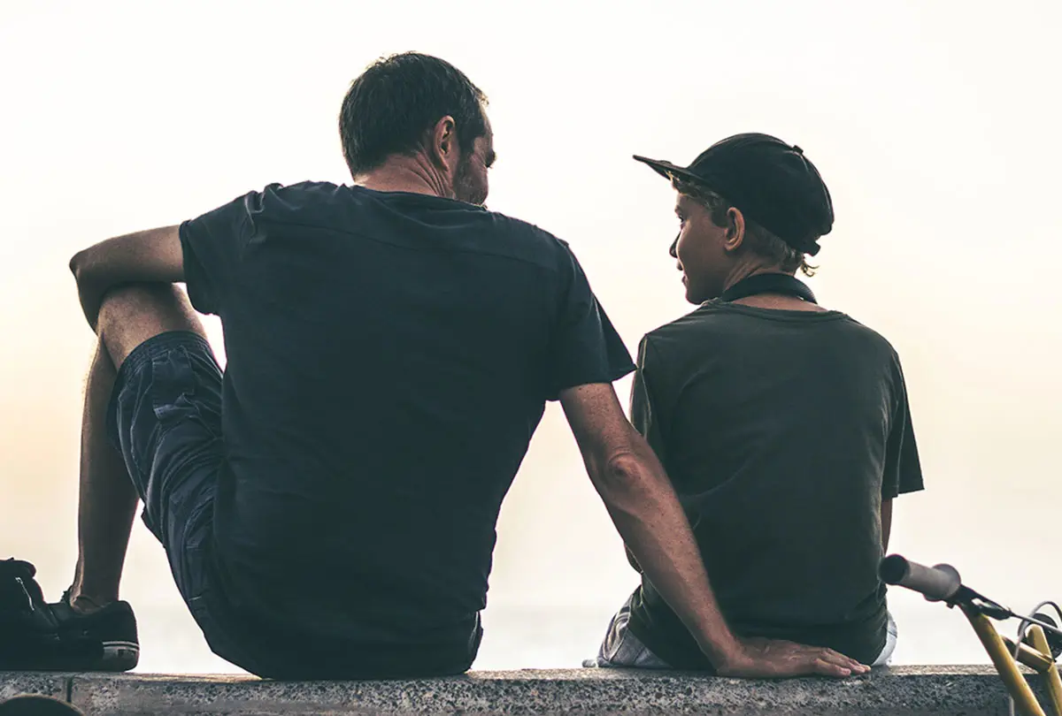 A man and a boy sit together on a ledge, enjoying a moment of ...
